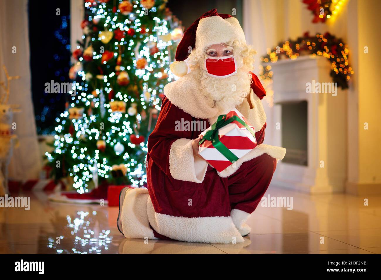 Santa Claus in face mask brings presents at Christmas tree and ...