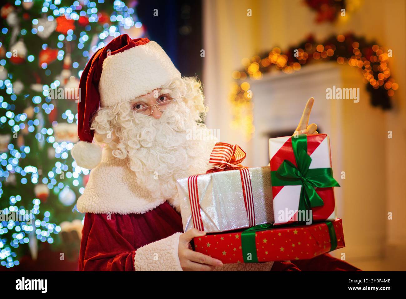 Santa Claus delivering gifts on Christmas eve. Presents under Xmas tree. Decorated living room ...