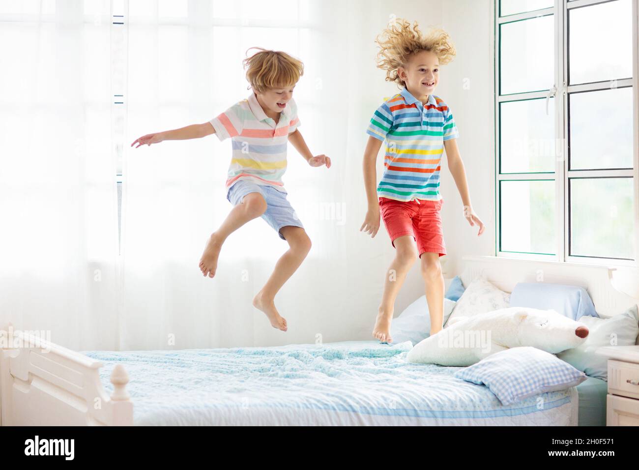 Child jumping on bed in white bedroom with big window. Kids play at ...