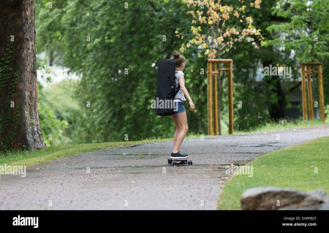 Young girl with musical instrument on her back riding skateboard in ...