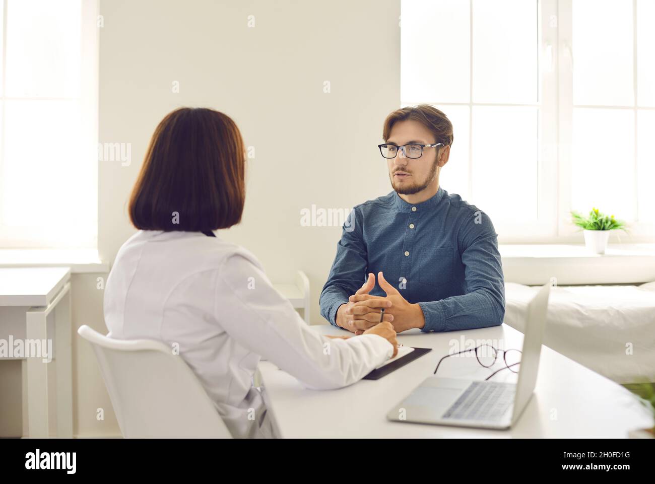 Young man having conversation with doctor while visiting hospital for ...