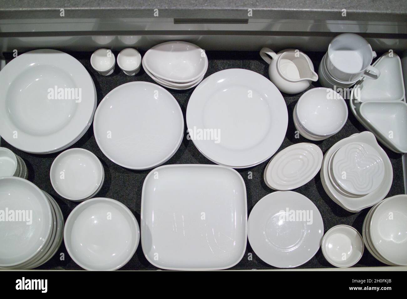 Minimalistic white crockery organised in large storage drawers in a ...