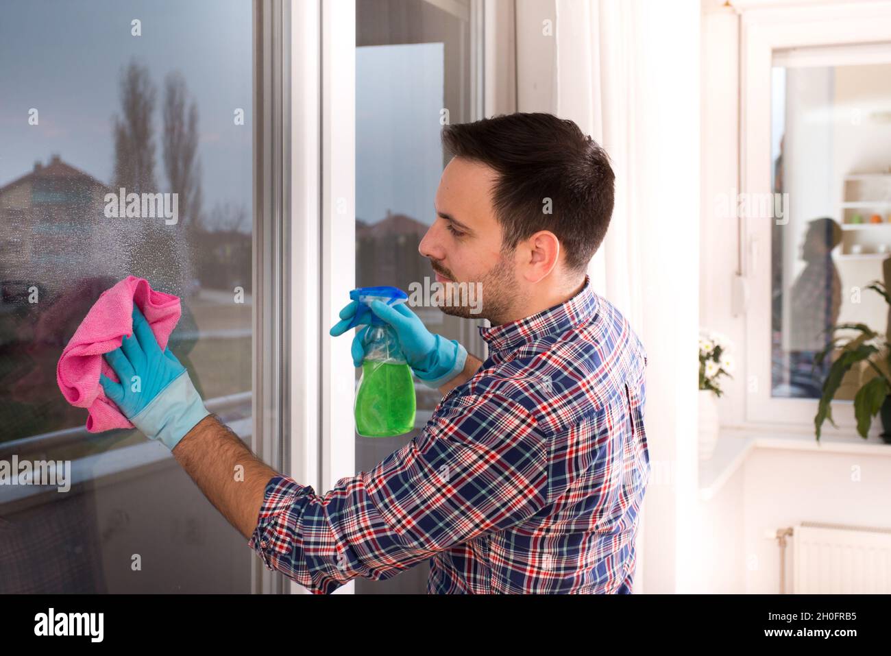 Handsome young man cleaning windows with cloth and spray bottle at home ...