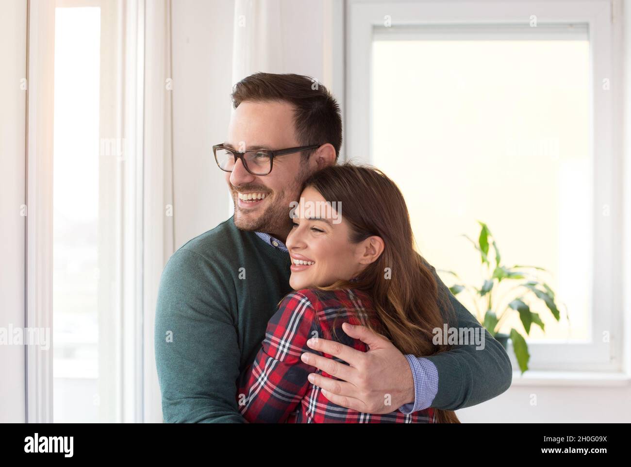 Happy young couple in love standing in hug beside window at home Stock ...
