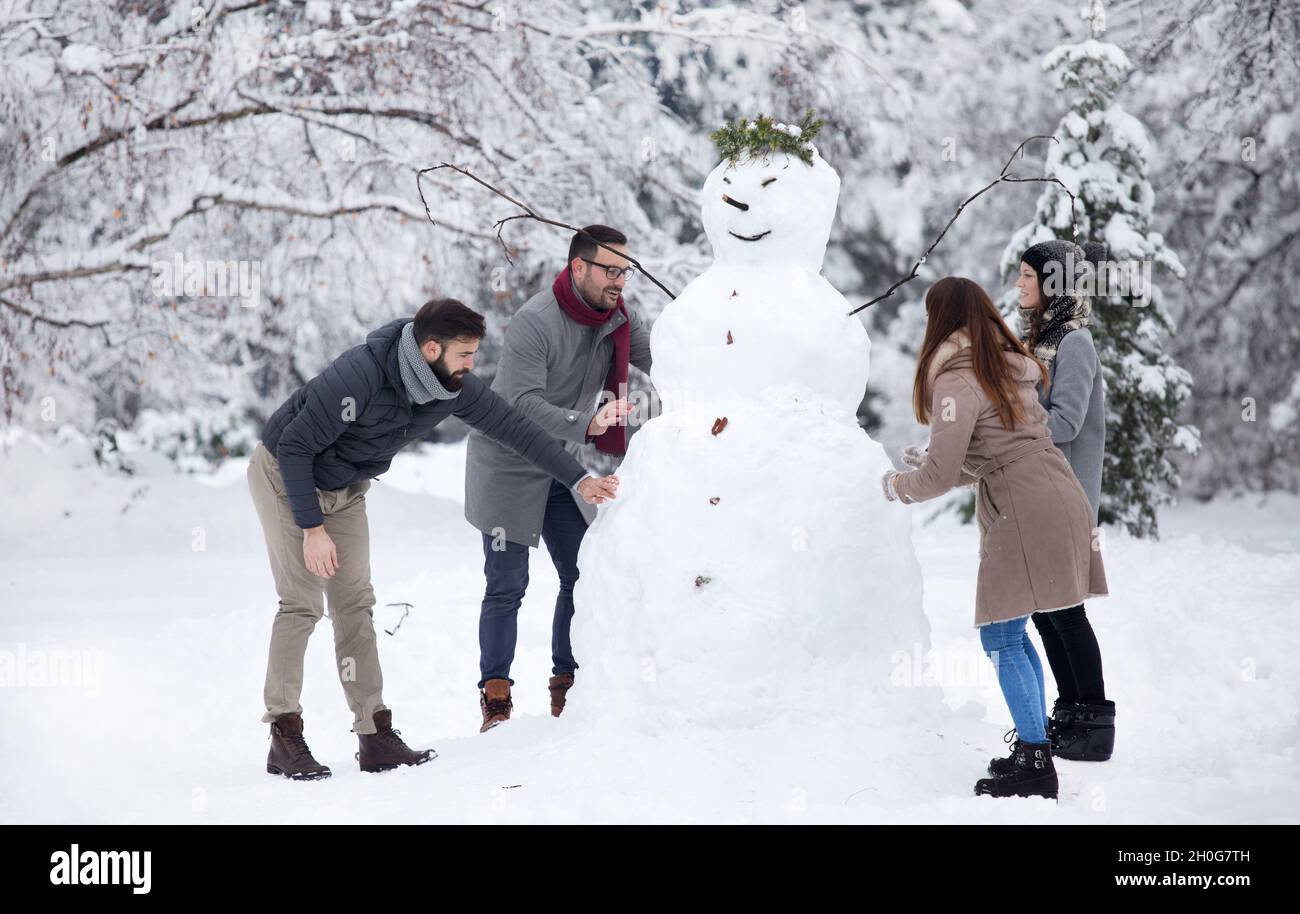Two young couples having fun by building big snowman in park during ...