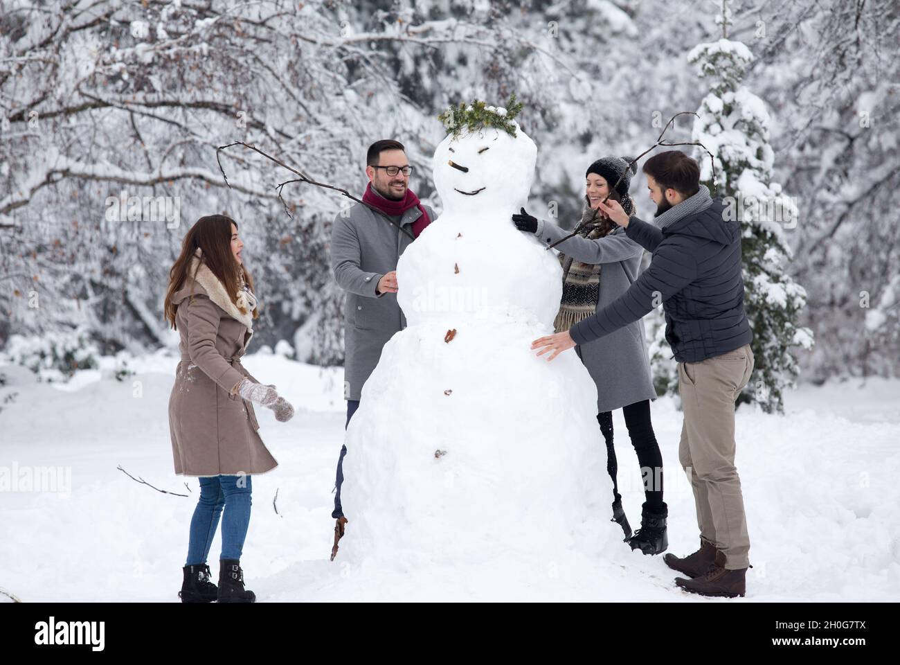 Two young couples having fun by building big snowman in park during ...