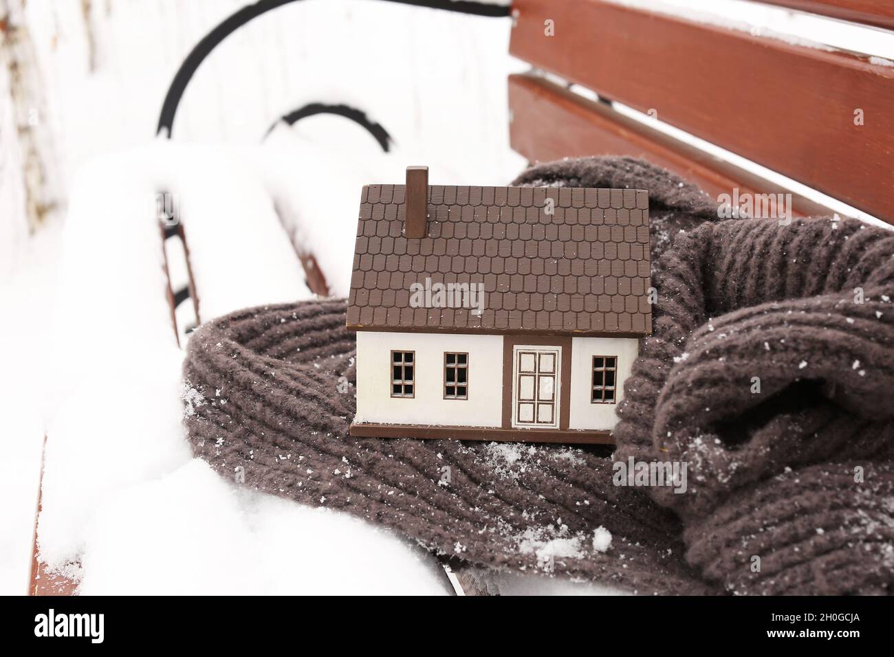 Figure of house and scarf on snow-covered bench. Concept of heating ...
