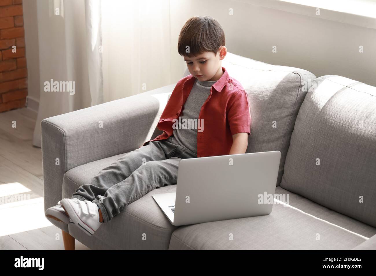 Little boy watching cartoons with laptop on sofa in living room Stock ...