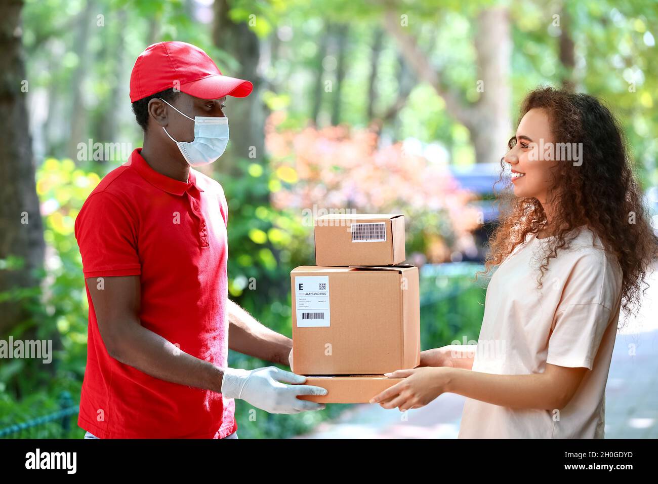 African-American woman receiving parcel from delivery man outdoors ...