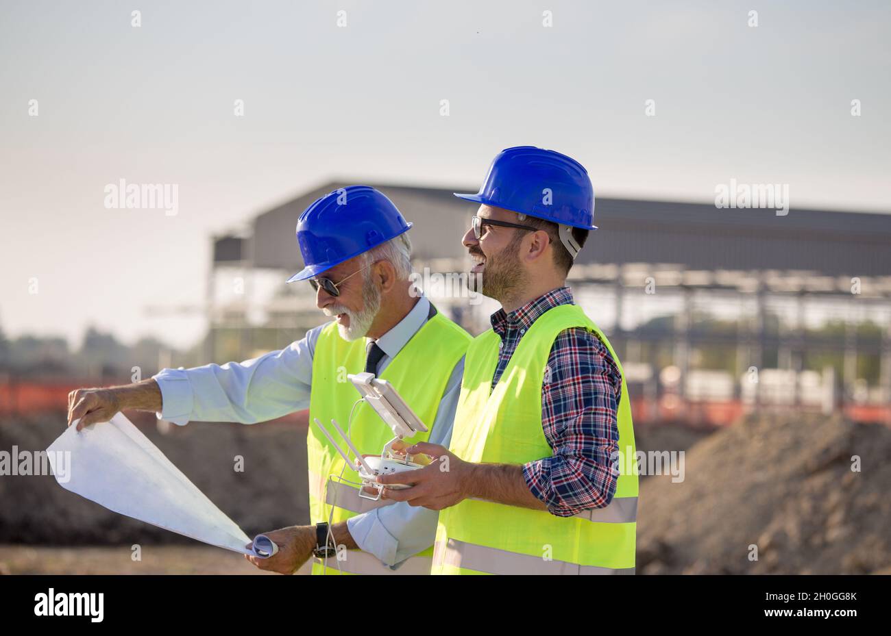 Two engineers with helmets and vests operating with drone by remote ...