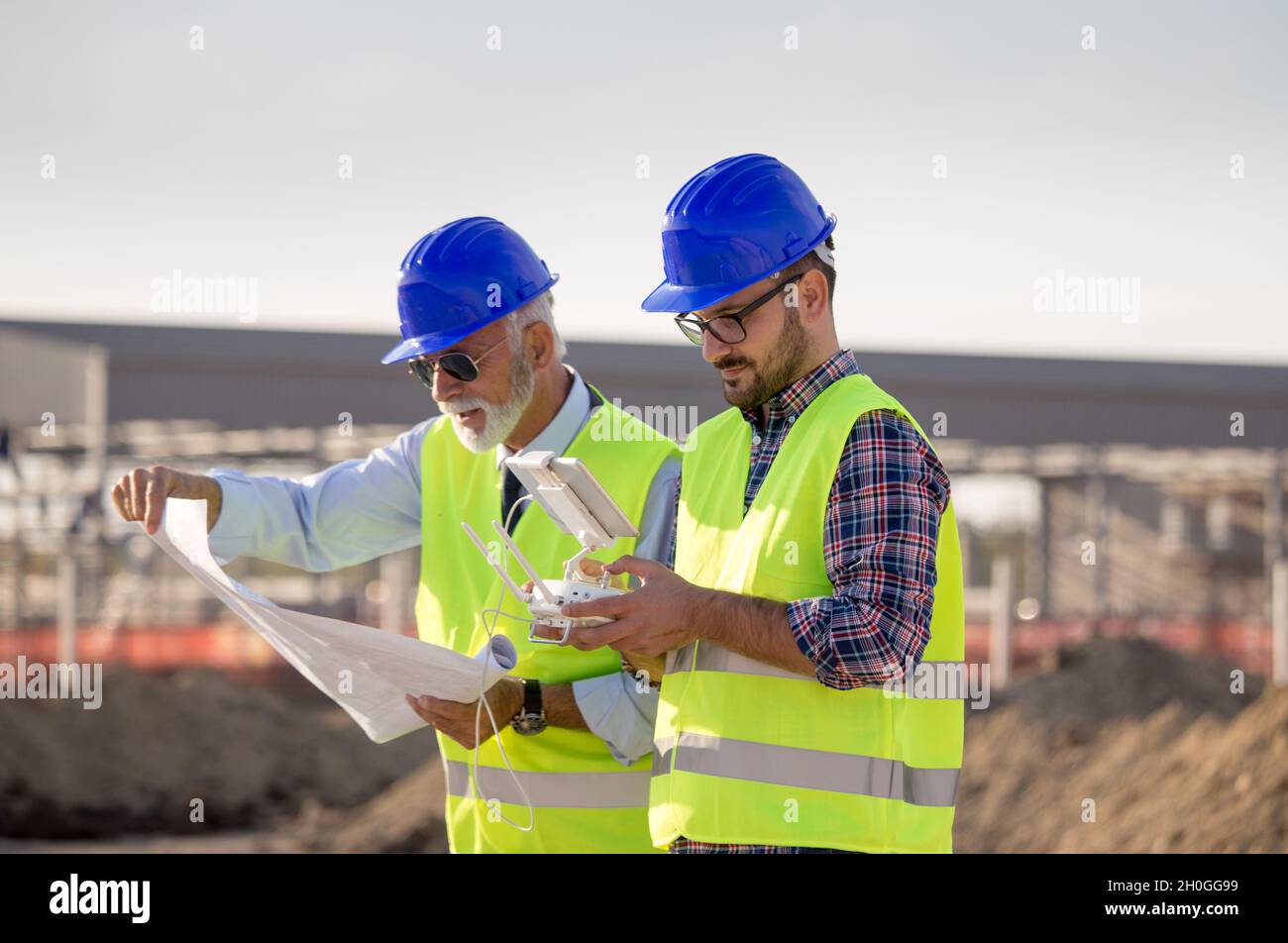 Two engineers with helmets and vests operating with drone by remote ...