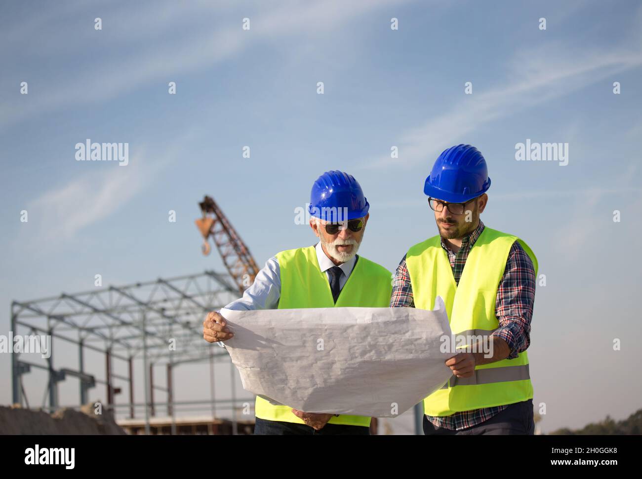 Two engineers talking at building site with metal construction in ...