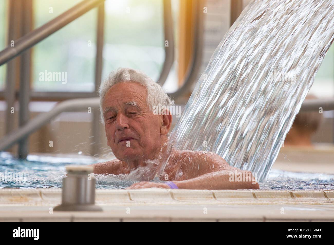 Elderly man enjoying in pool with hot water and massaging shower in spa ...