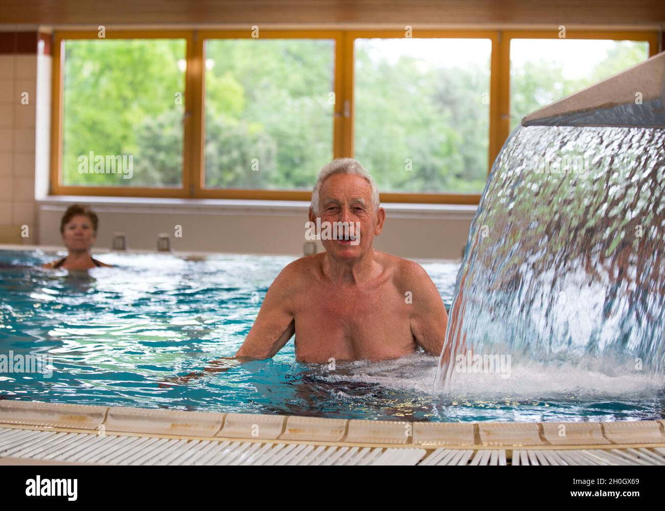 Elderly man enjoying in pool with hot water and massaging shower in spa ...
