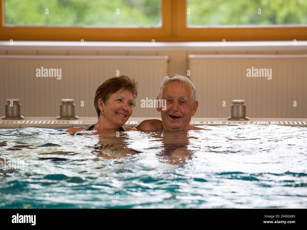 Elderly couple enjoying in indoor pool with hot water in spa resort ...