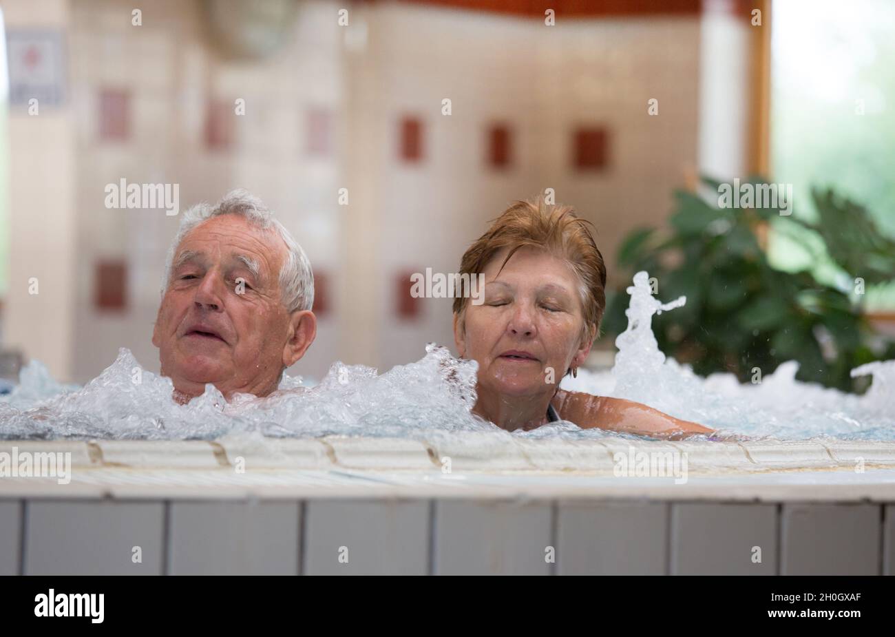 Elderly couple enjoying in indoor pool with hot water in spa resort ...