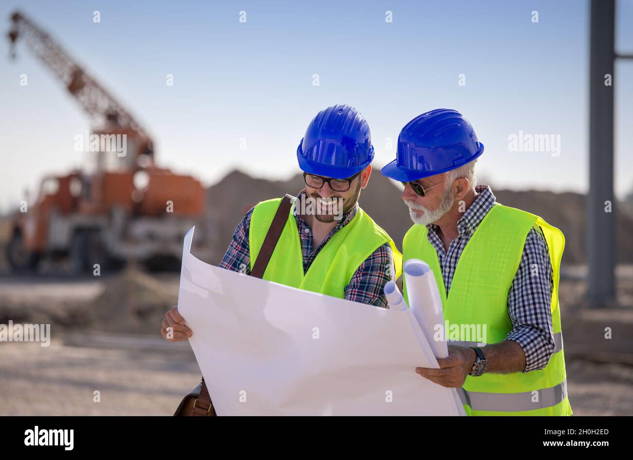 Two satisfied engineers looking at blueprints at building site with ...