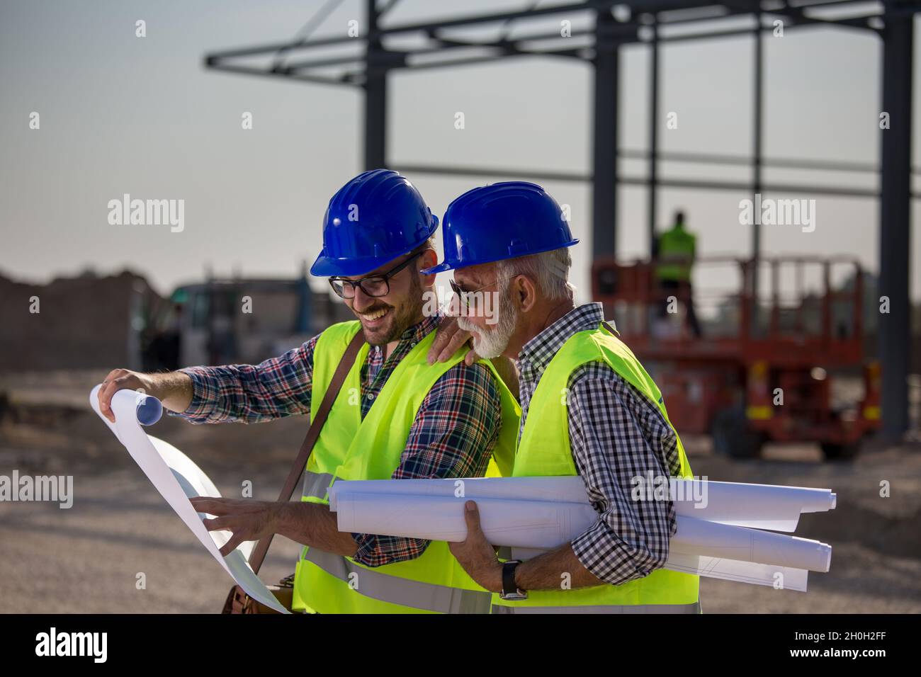 Two satisfied engineers looking at blueprints at building site with ...