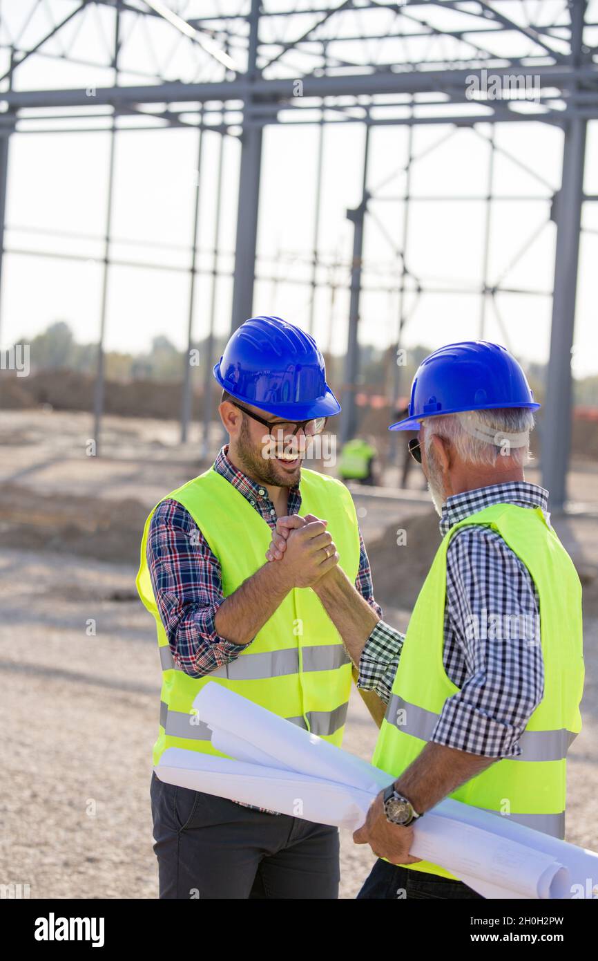 Two engineers shaking hands on building site with metal construction in ...