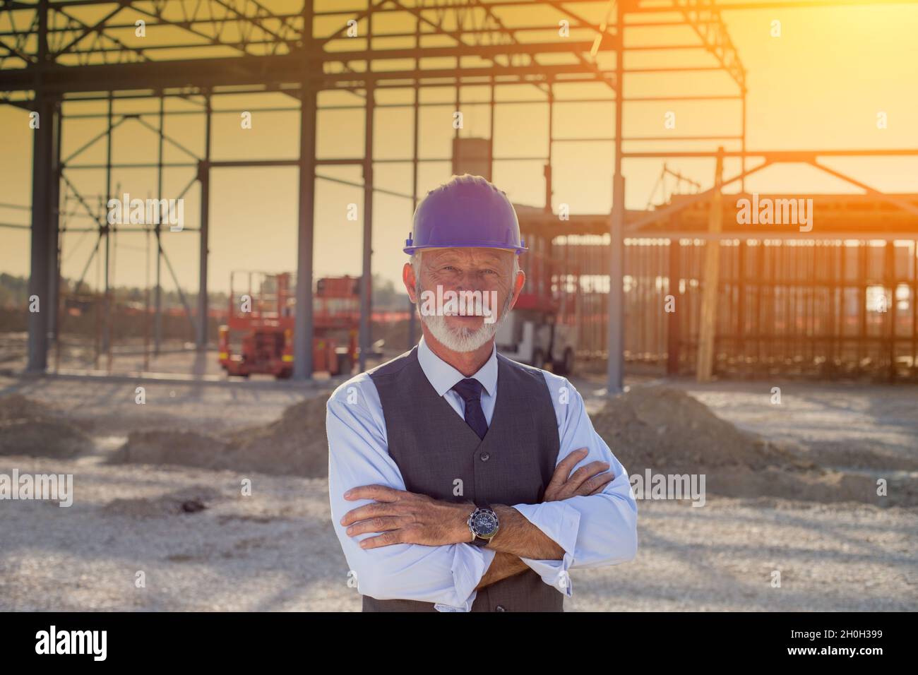 Portrait of foreman with helmet and vest in front of metal structure on ...