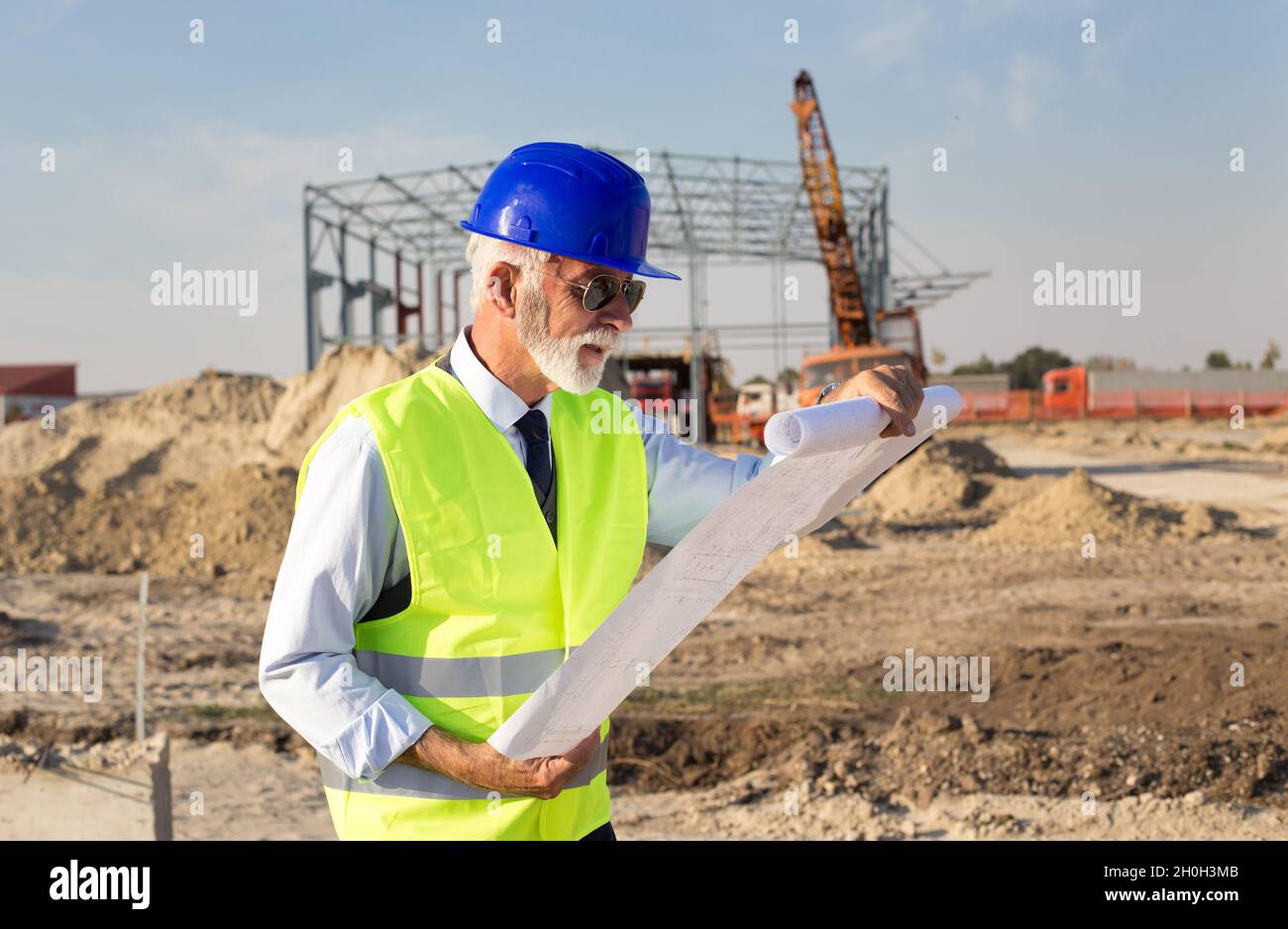 Senior engineer looking at blueprints in front of metal construction at ...