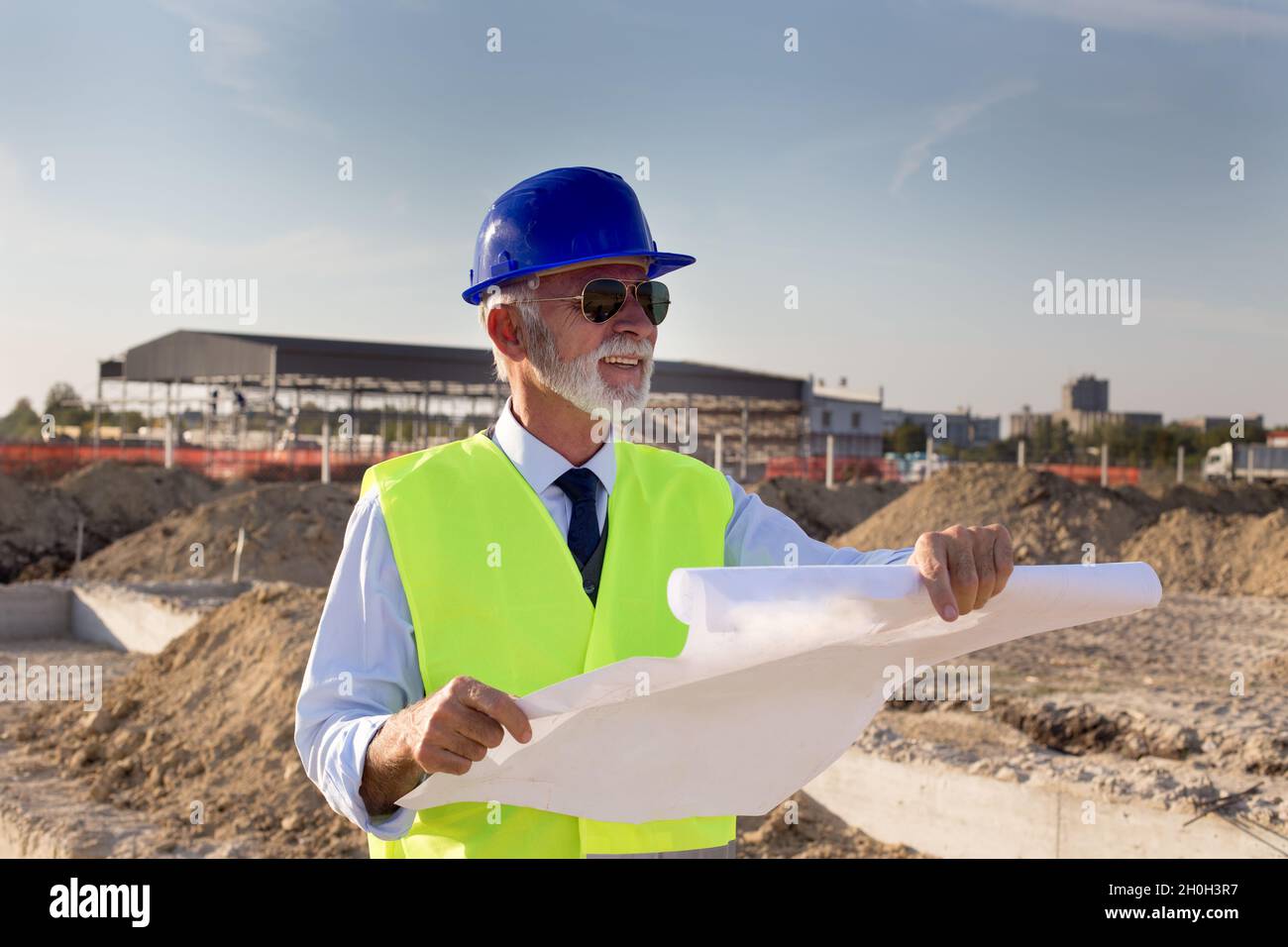 Senior engineer looking at blueprints in front of metal construction at ...