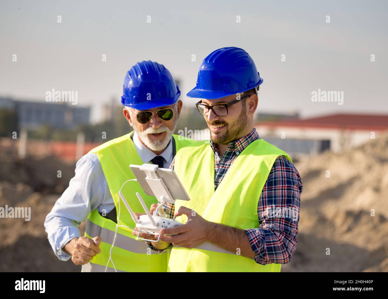 Two engineers with helmets and vests operating with drone by remote ...