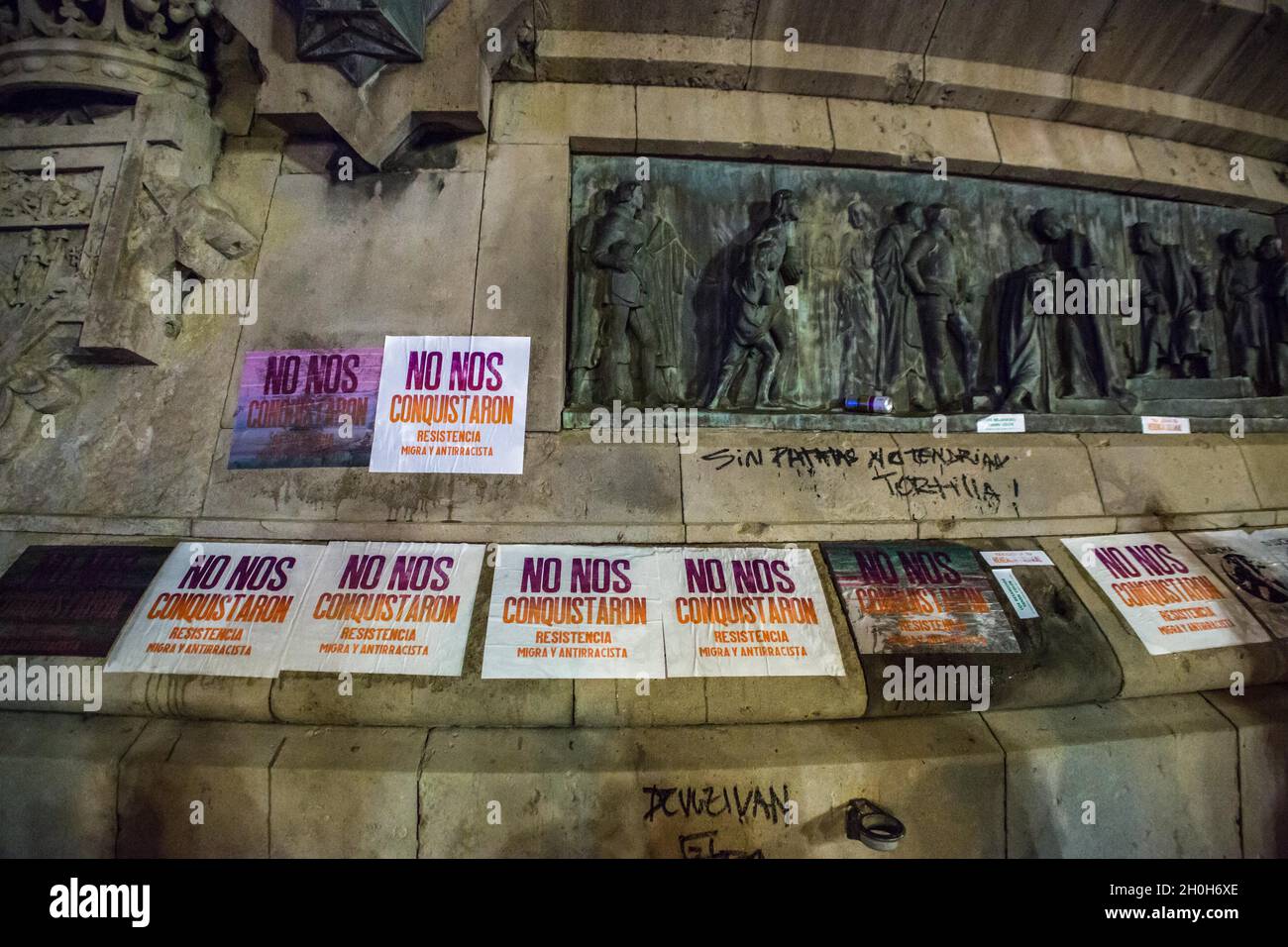 Posters are seen glued to the Christopher Columbus monument that read ...