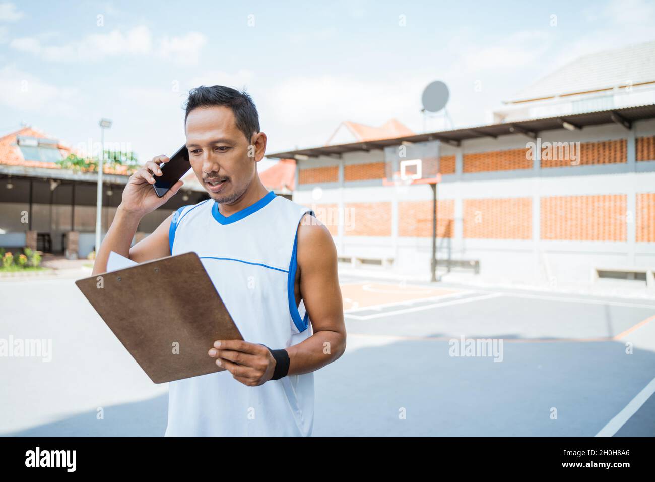 a basketball coach calls using a mobile phone while holding a clipboard ...