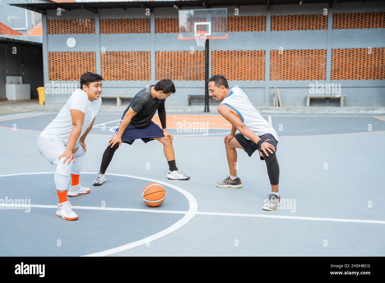 three basketball players stretching their legs while warming up before ...