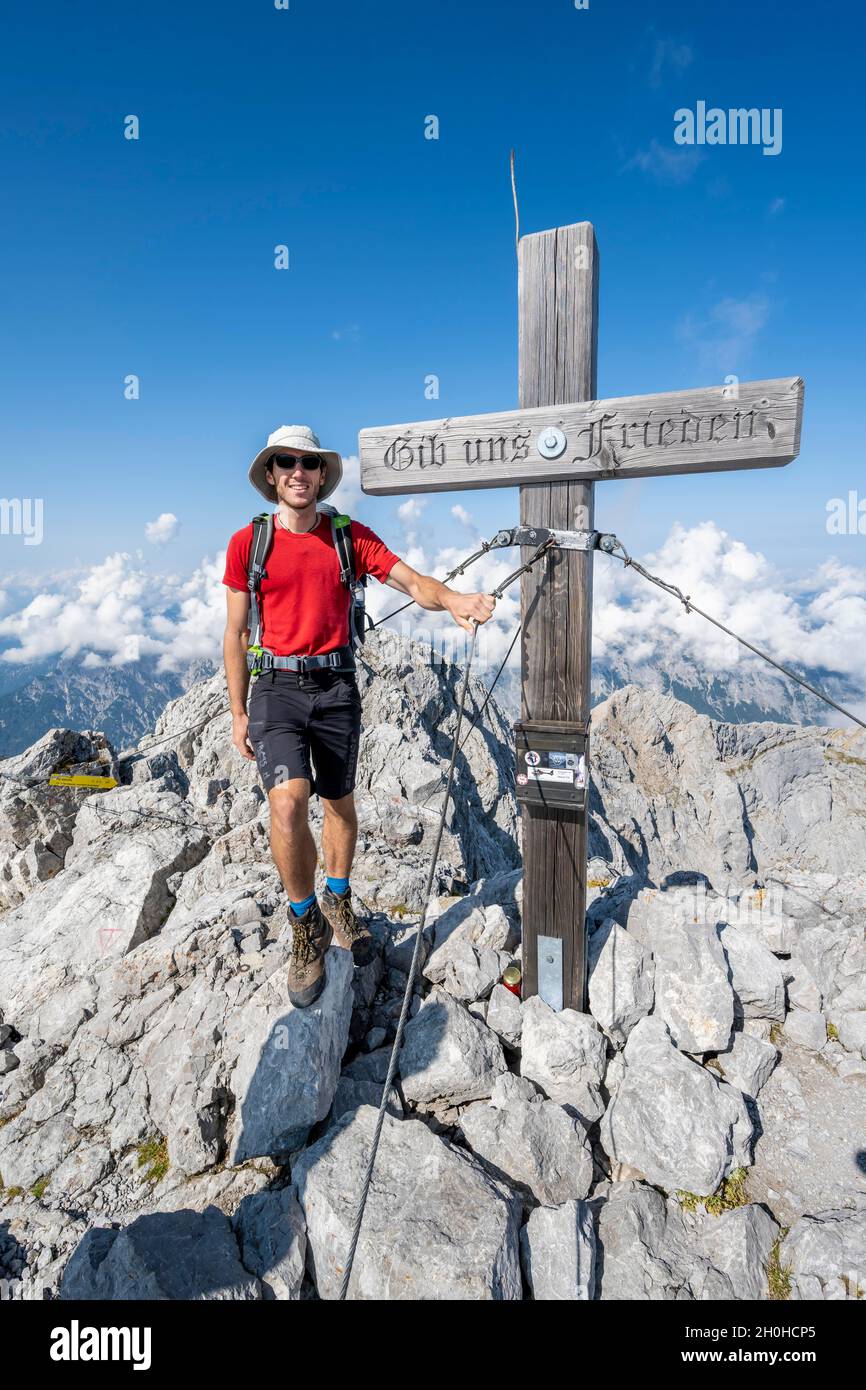 Hiker at the summit cross of the Hochkalter, Berchtesgaden Alps ...