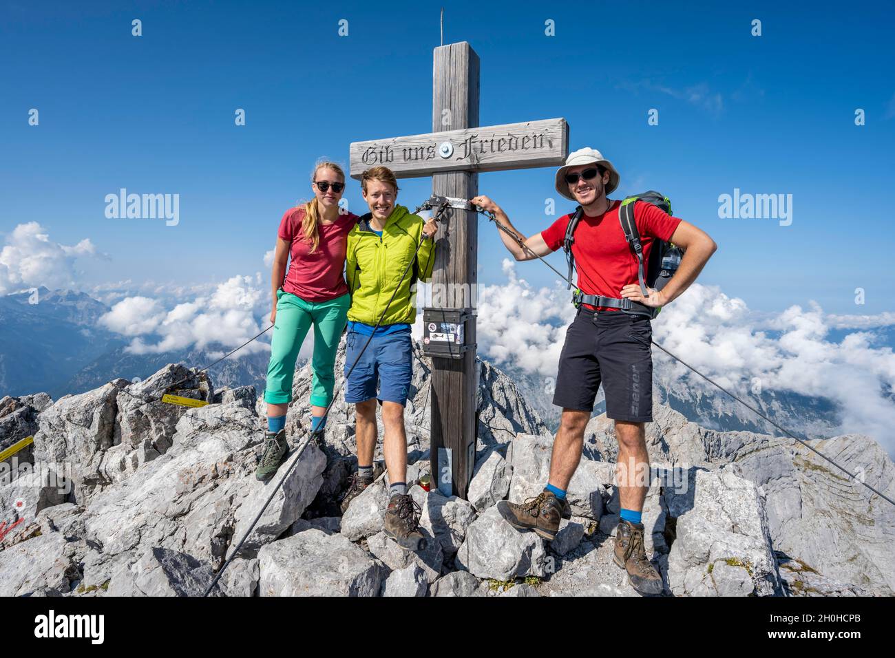 Three hikers at the summit cross of the Hochkalter, Berchtesgaden Alps ...