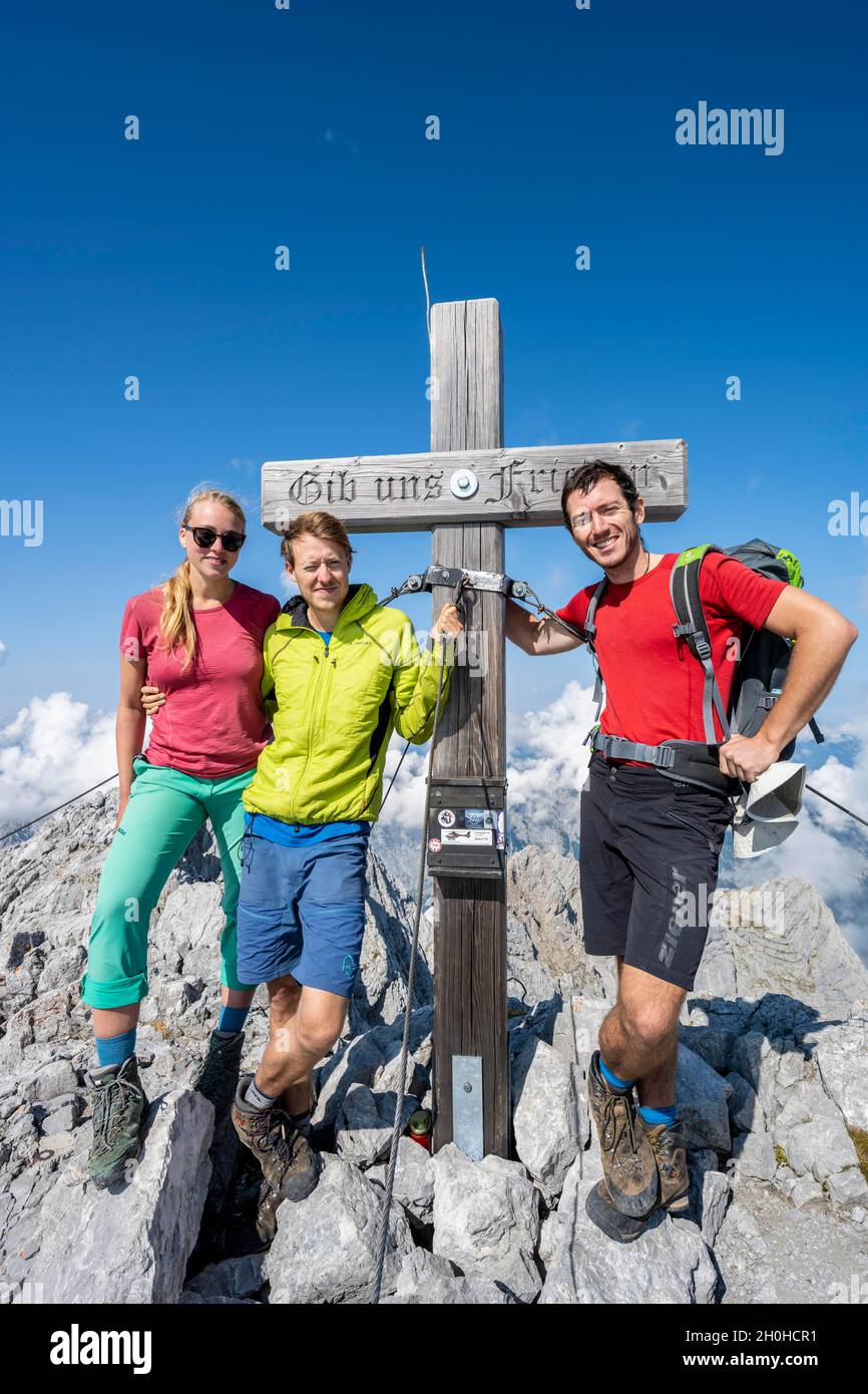 Three hikers at the summit cross of the Hochkalter, Berchtesgaden Alps ...