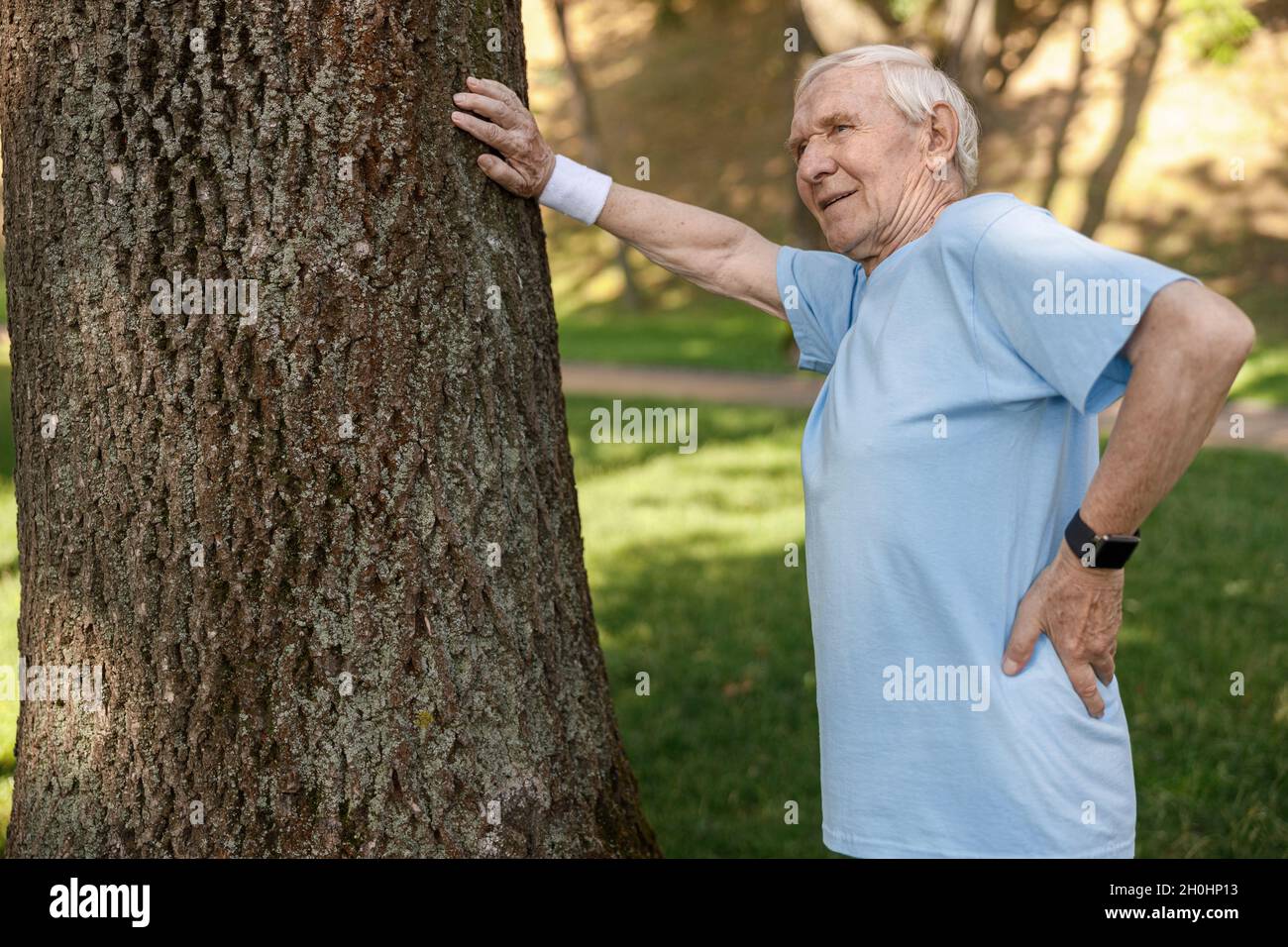 Positive senior sportsman rests leaning onto tree trunk at training in ...