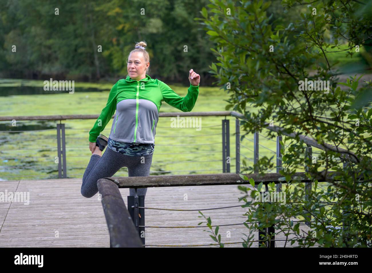 Sporty fit middle-aged woman doing stretching exercises on a wooden ...