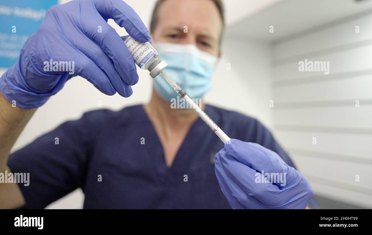 wide shot of a male healthcare worker filling a syringe with a covid-19 ...