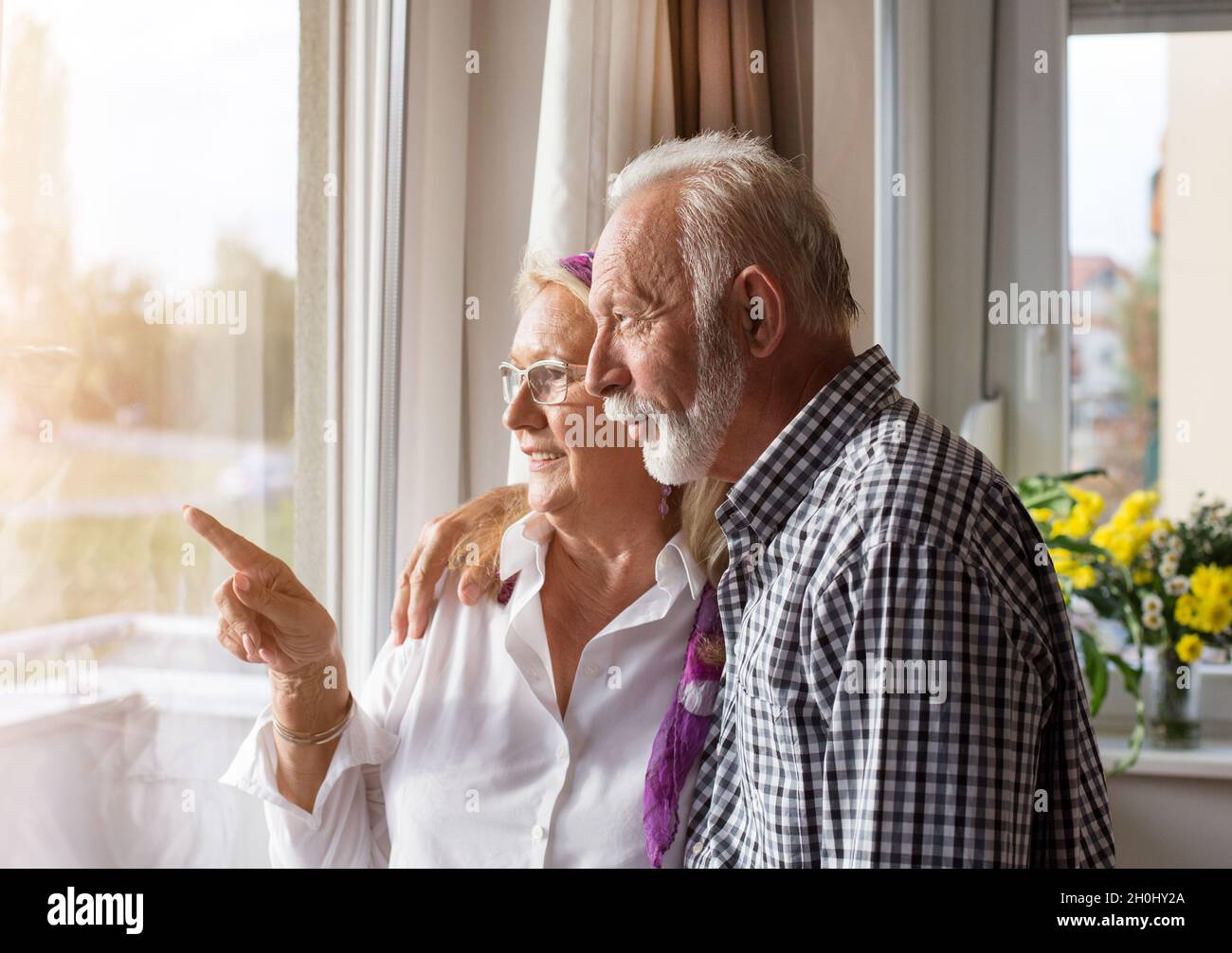 Happy senior couple standing beside window and looking out Stock Photo ...