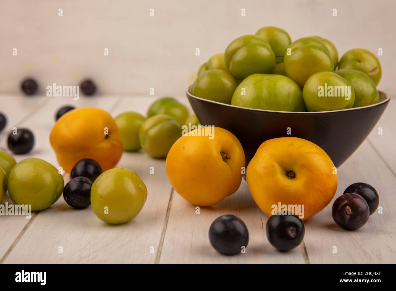 side view of green cherry plums on a bowl with fruits such as ...