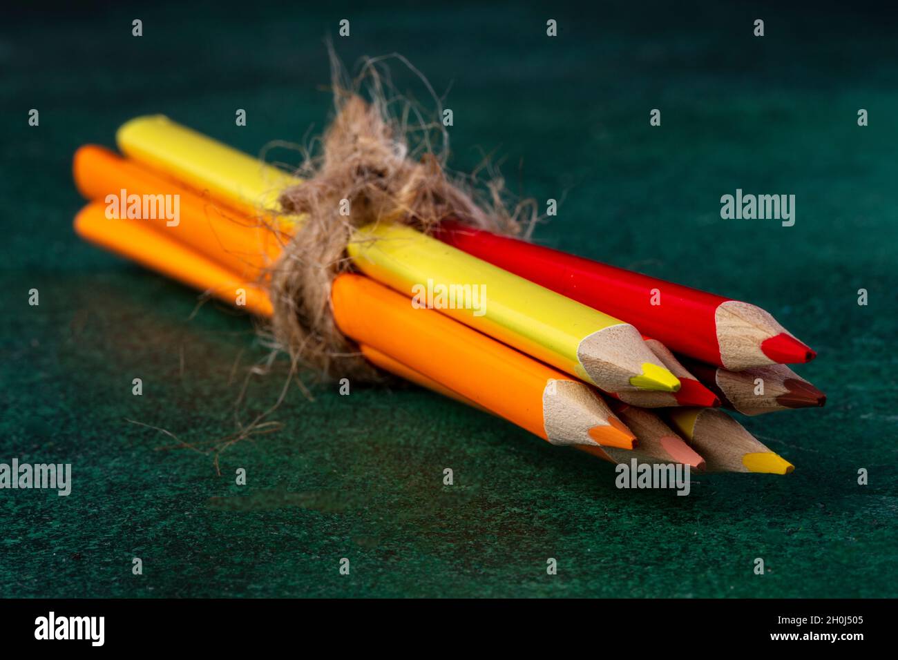 side view of colored pencils tied with a rope on dark green background ...