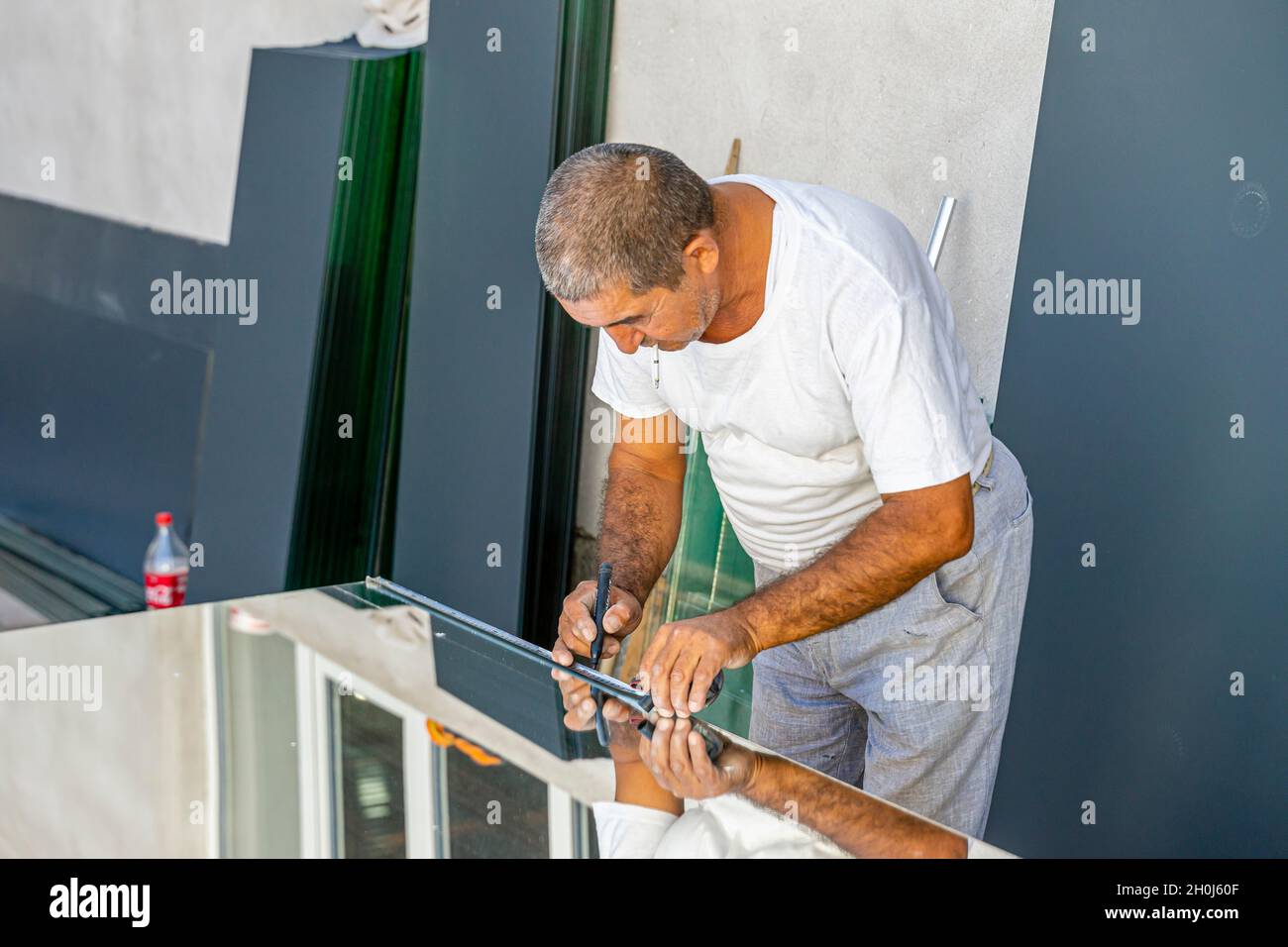 A man is measuring mirror glass with a ruler to cut it for using in the ...