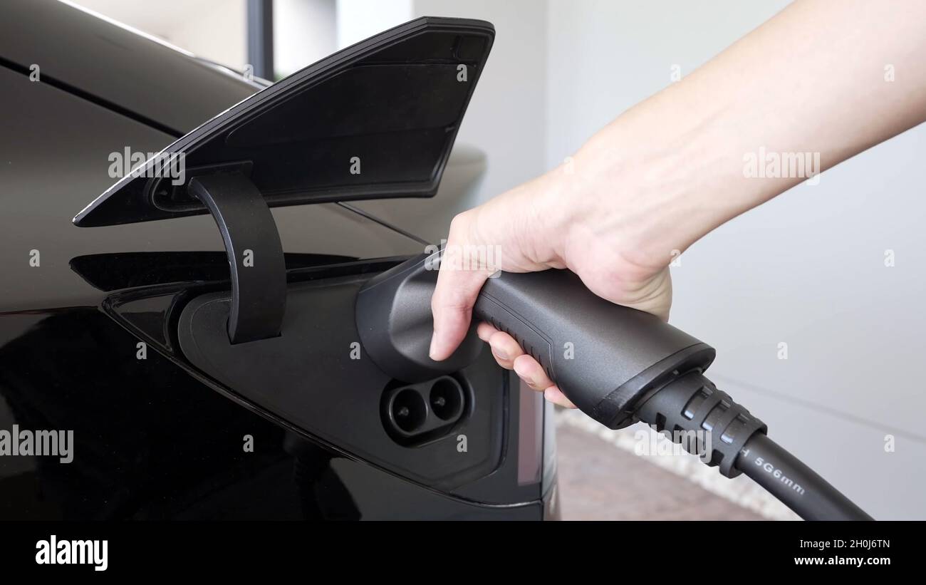 Close-up of an arm inserting an electric car charger into a black ...