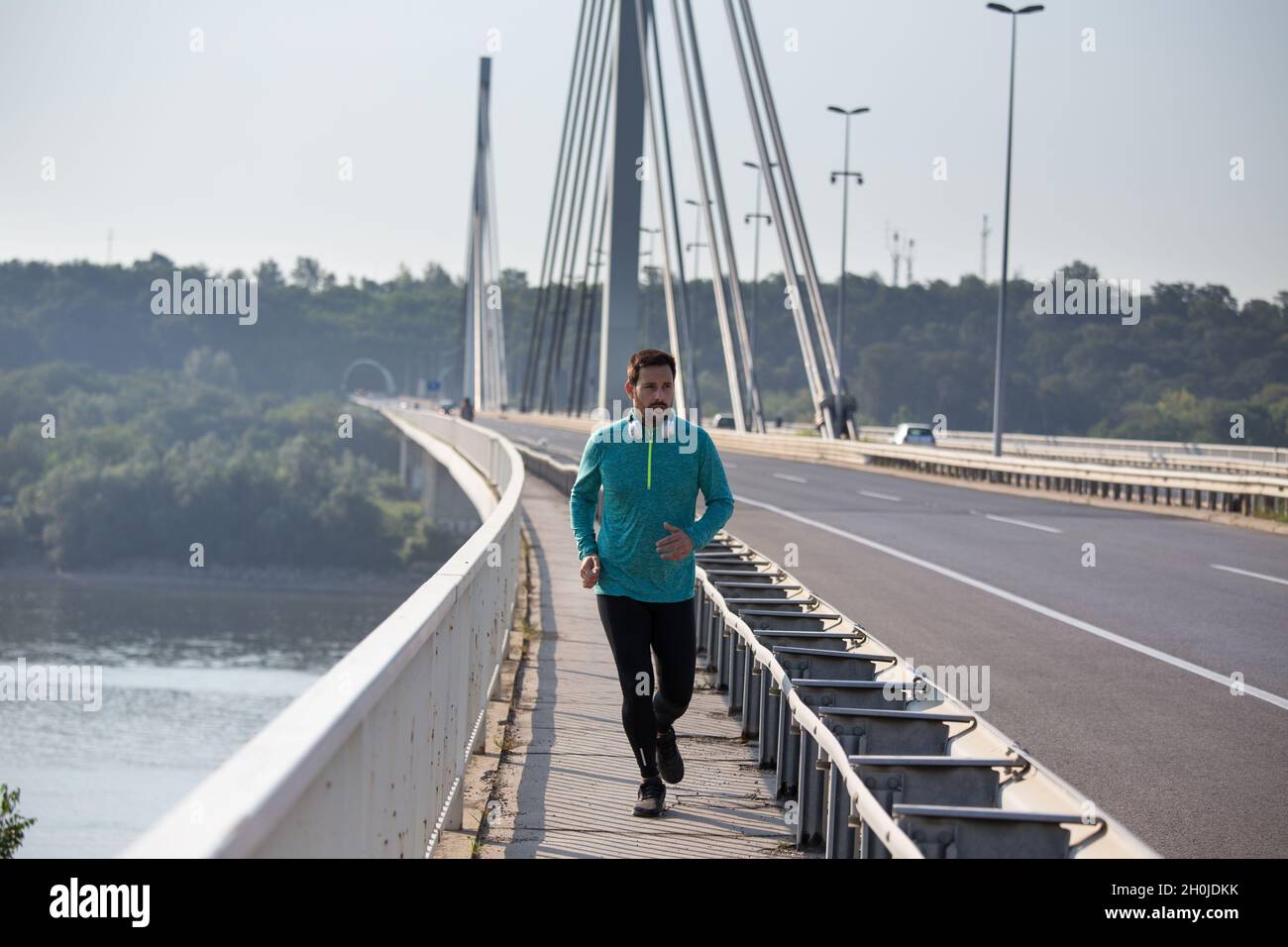 Handsome man running on bridge with forest in background. Urban morning ...