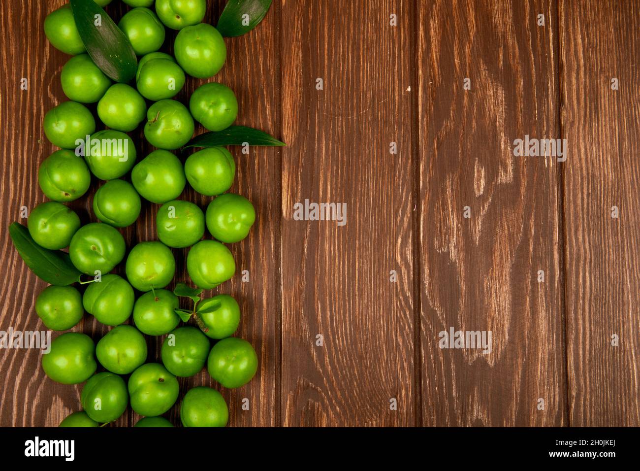 top view of sour green plums with ruscus leaves on wooden background ...