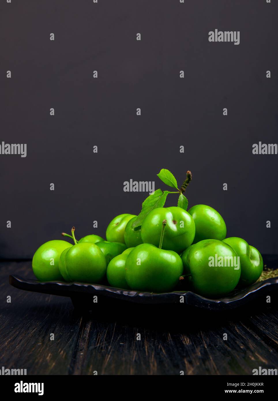 side view of sour green plums with dried peppermint on a black tray on ...