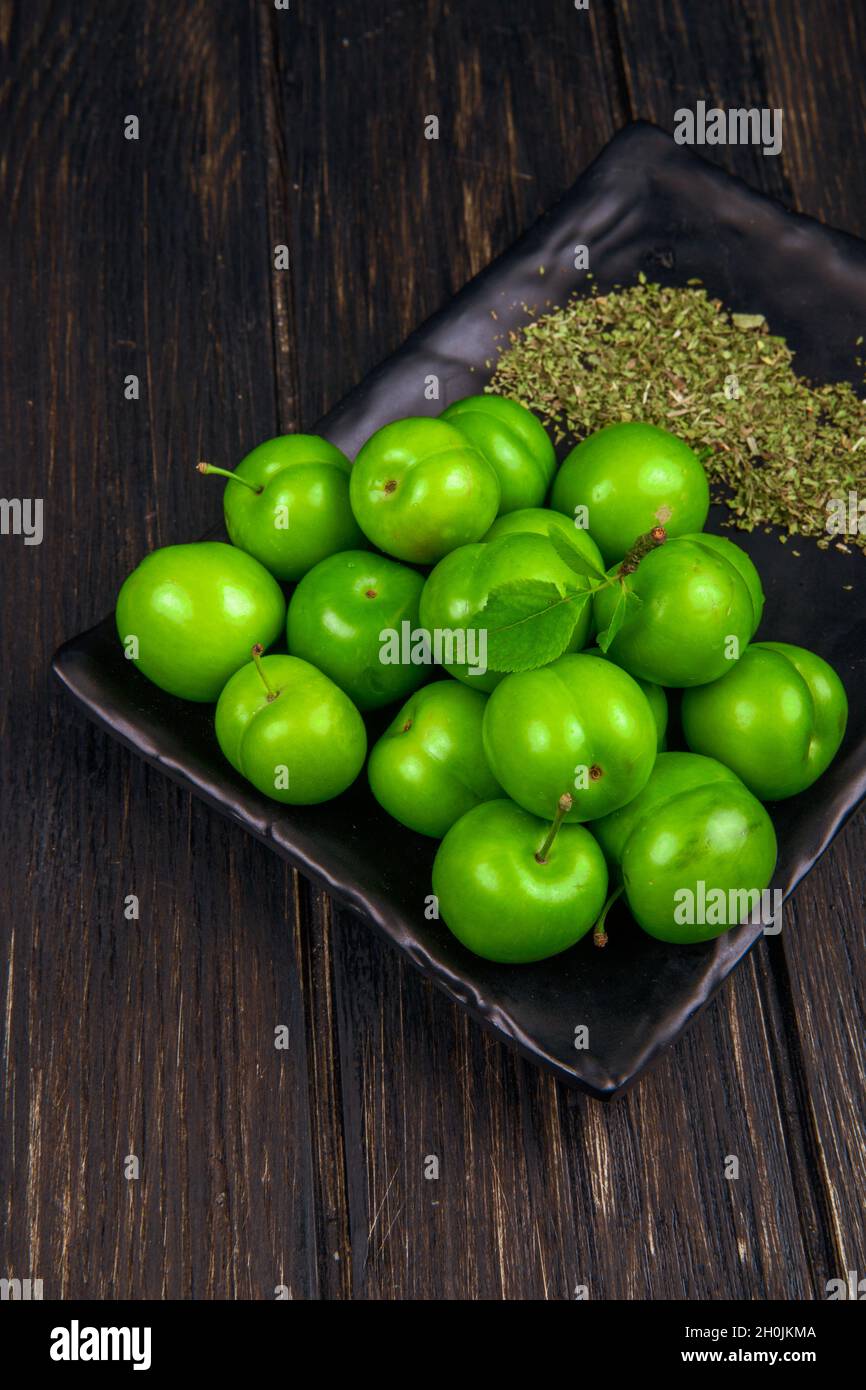 side view of sour green plums with dried peppermint on a black tray on ...