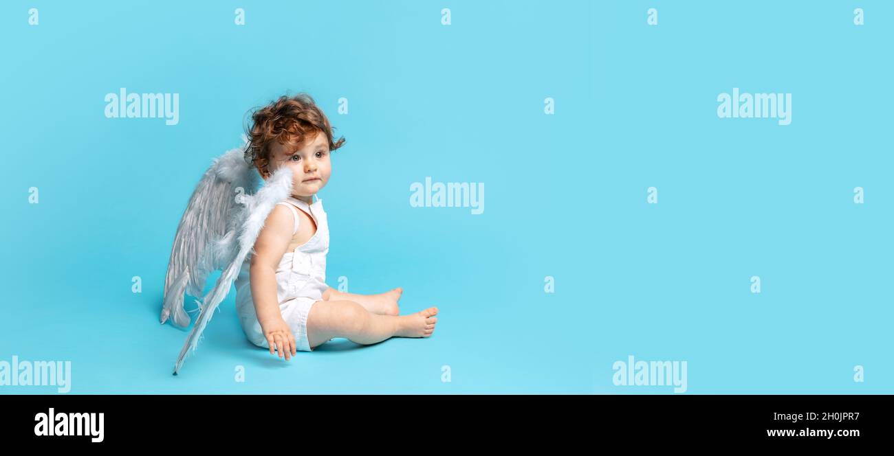 Side view portrait of cute toddler boy, baby in white romper with angel ...