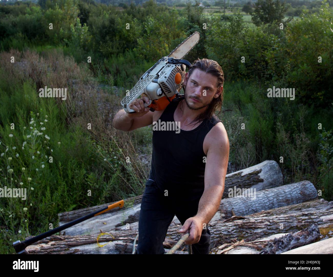 Young strong man lumberjack carrying chainsaw on shoulderand climbing ...