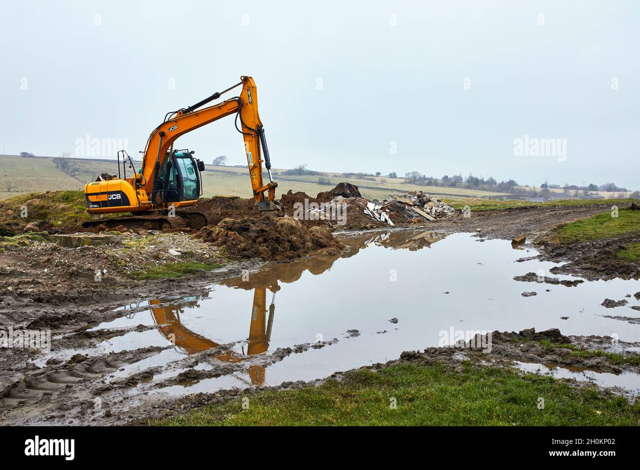At rest and with reflections in water filled tracks, a JCB digger ...