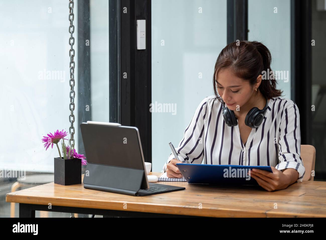 Asian woman taking notes in notebook and using laptop computer for e ...