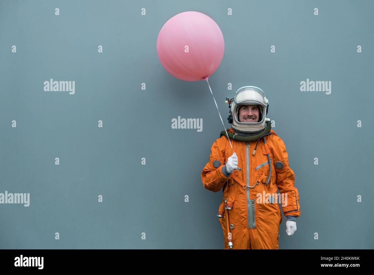 Astronaut wearing space suit and helmet holding pink inflatable balloon ...